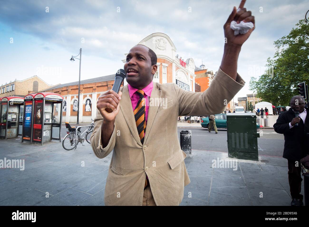 Street preacher of Brixton raises his hand and speak into a microphone ...