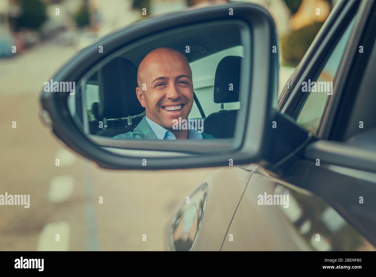 Happy handsome young business man driver in his car looking back to the ...