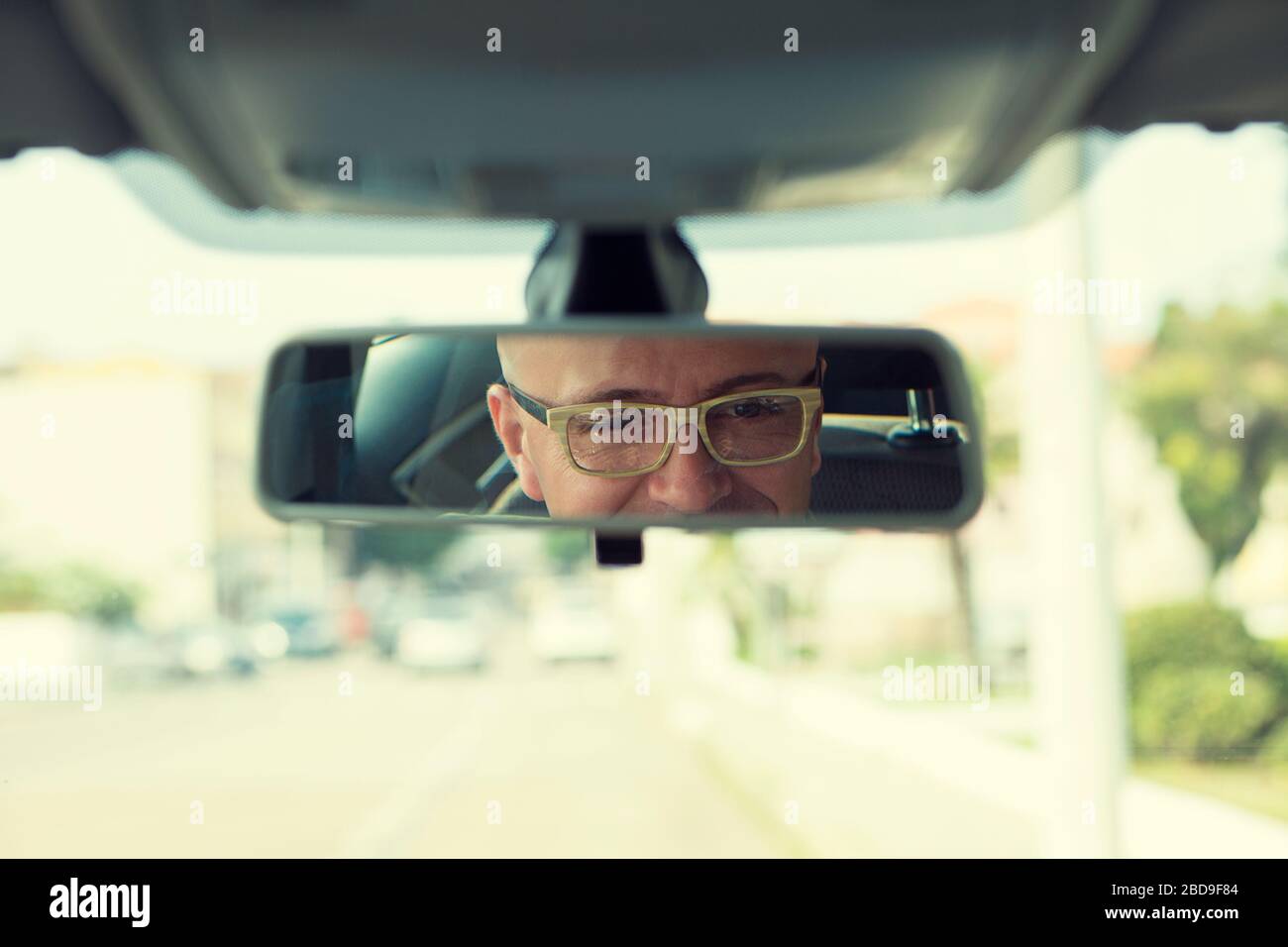 Closeup portrait, happy young man driver looking at rear view mirror ...