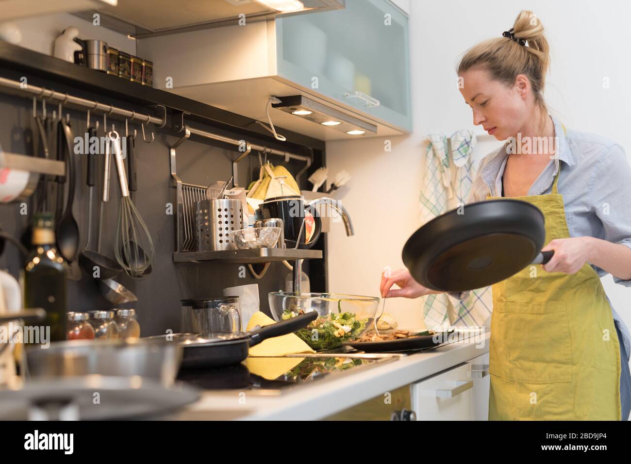 Stay at home housewife woman cooking in kitchen, stir frying dish in a ...