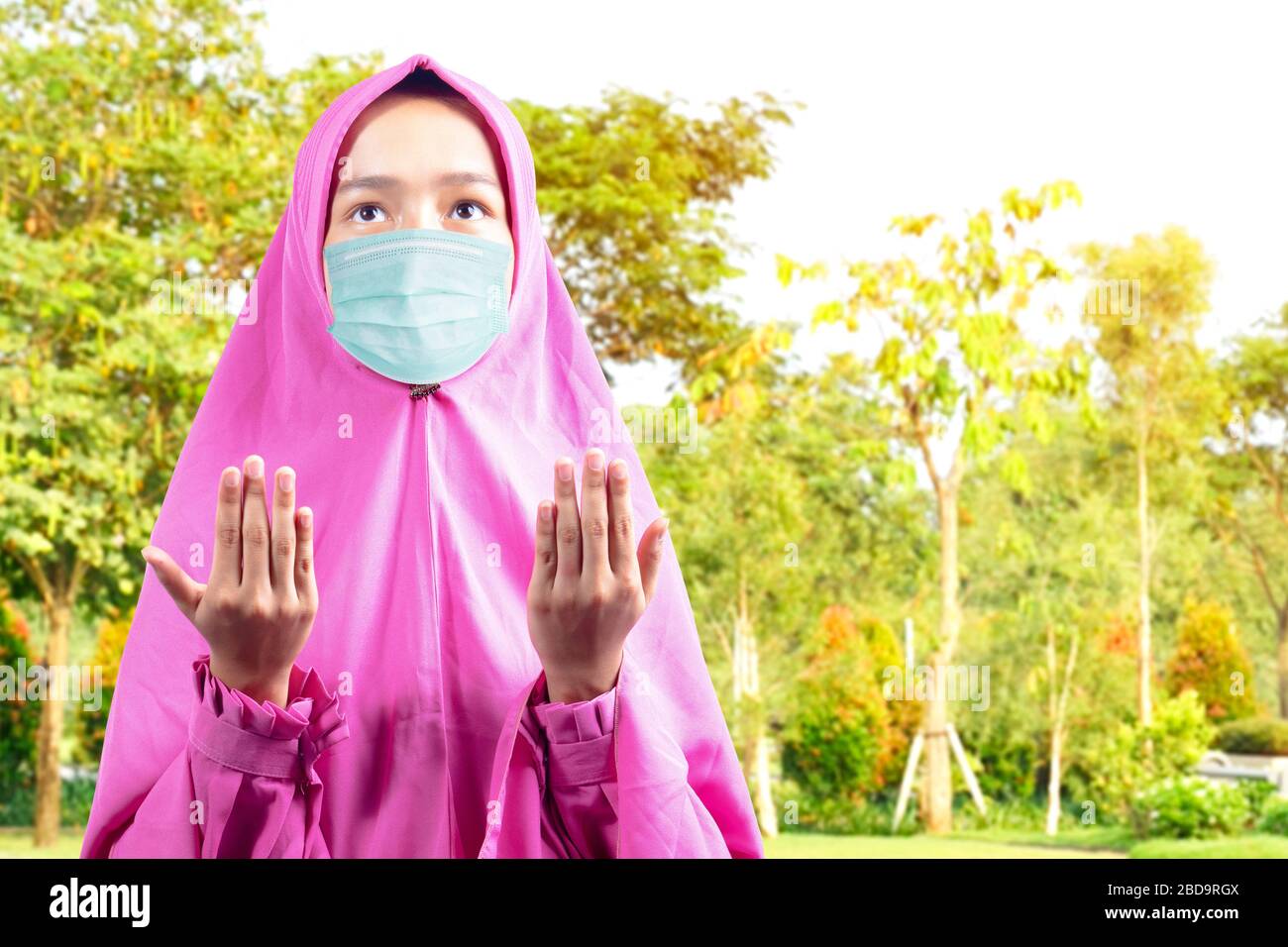 Asian Muslim woman in a veil and wearing flu mask standing while raised ...