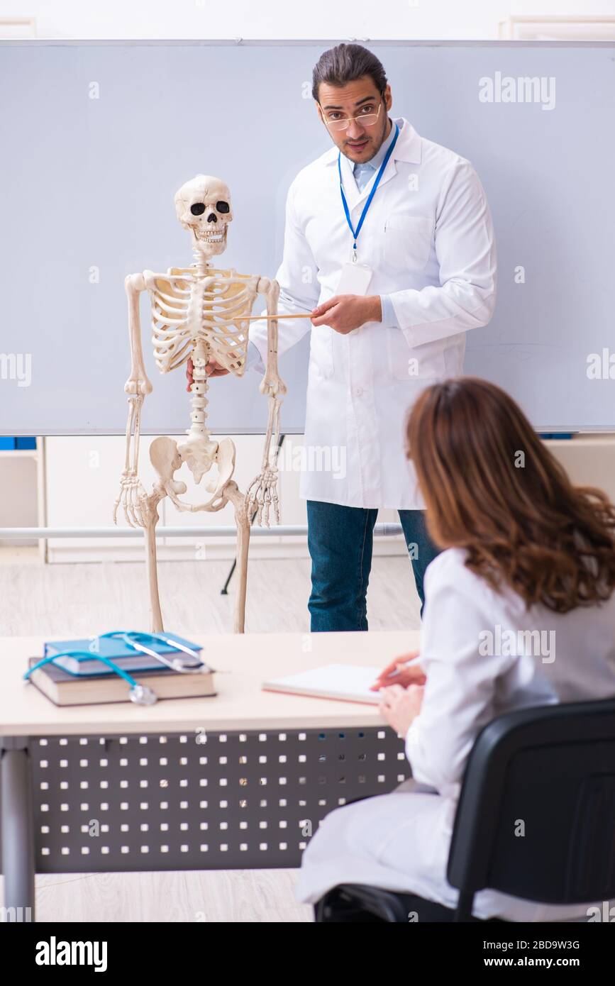 Young male teacher doctor, skeleton and female student in the classroom ...