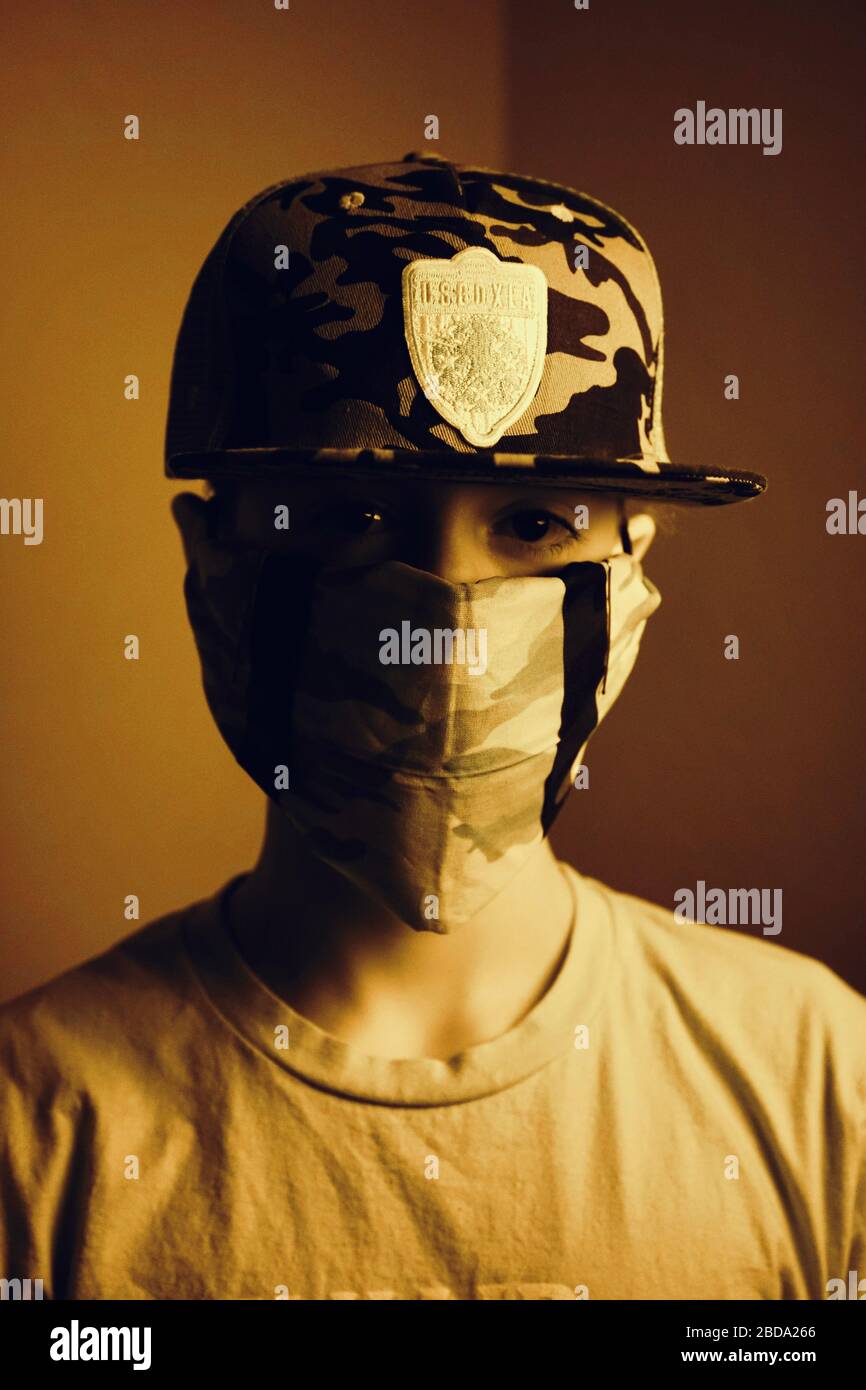 A teenage boy wears a camouflage hat and a homemade camouflage mask ...