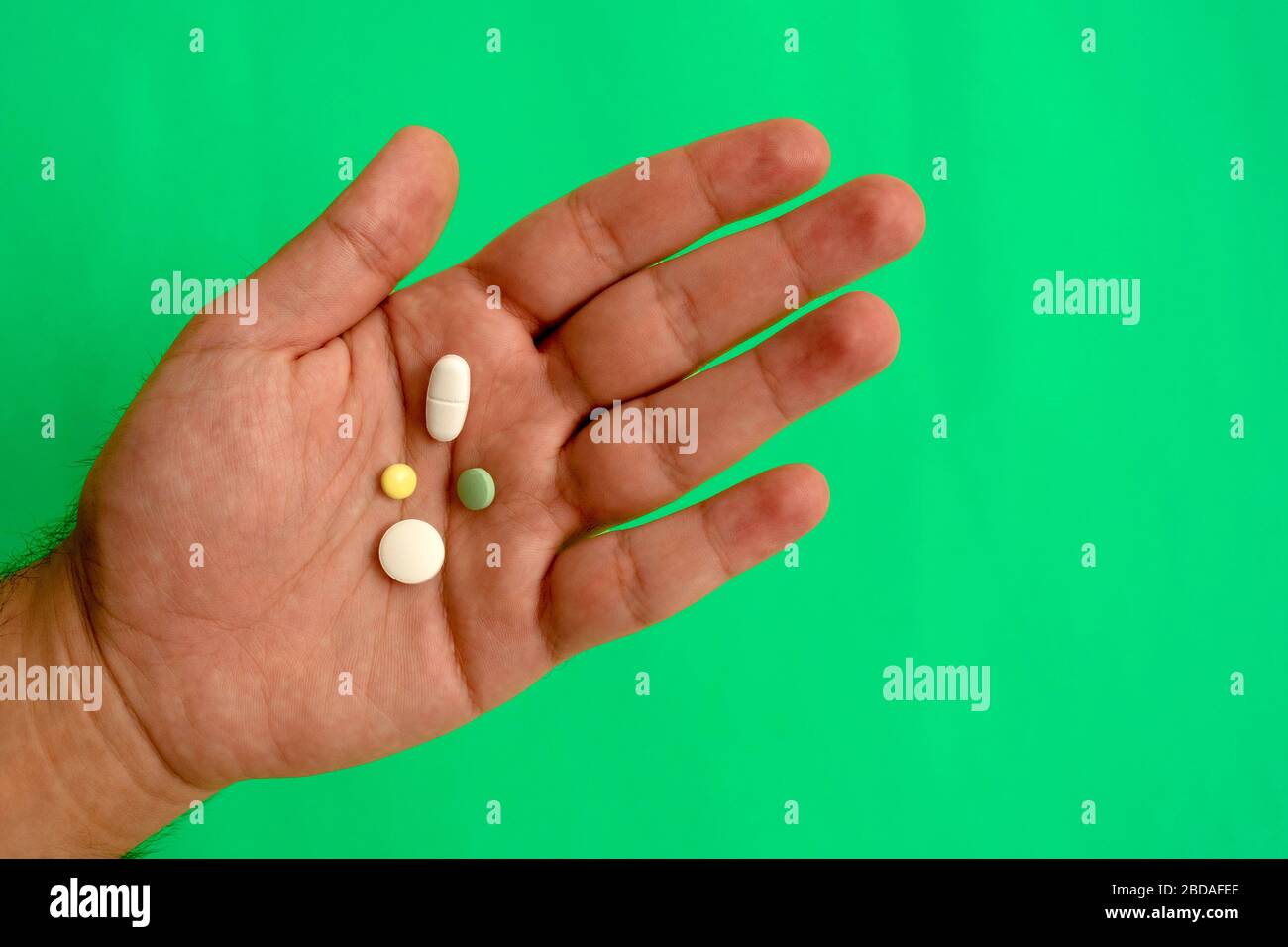 Man's hand with different pills on green background with copy space ...