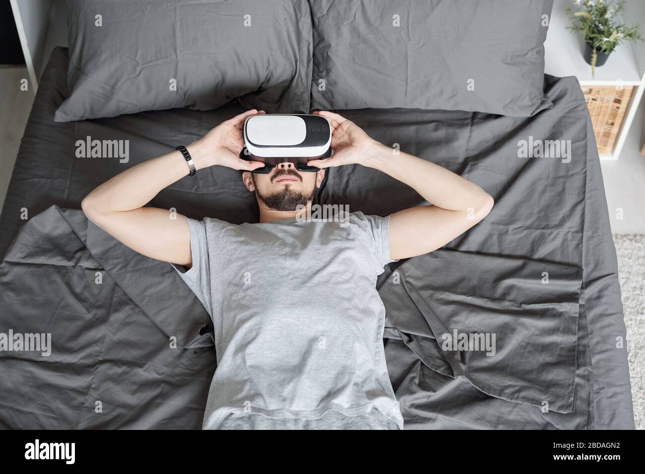 Above view of relaxed young bearded man lying in bed and using virtual ...