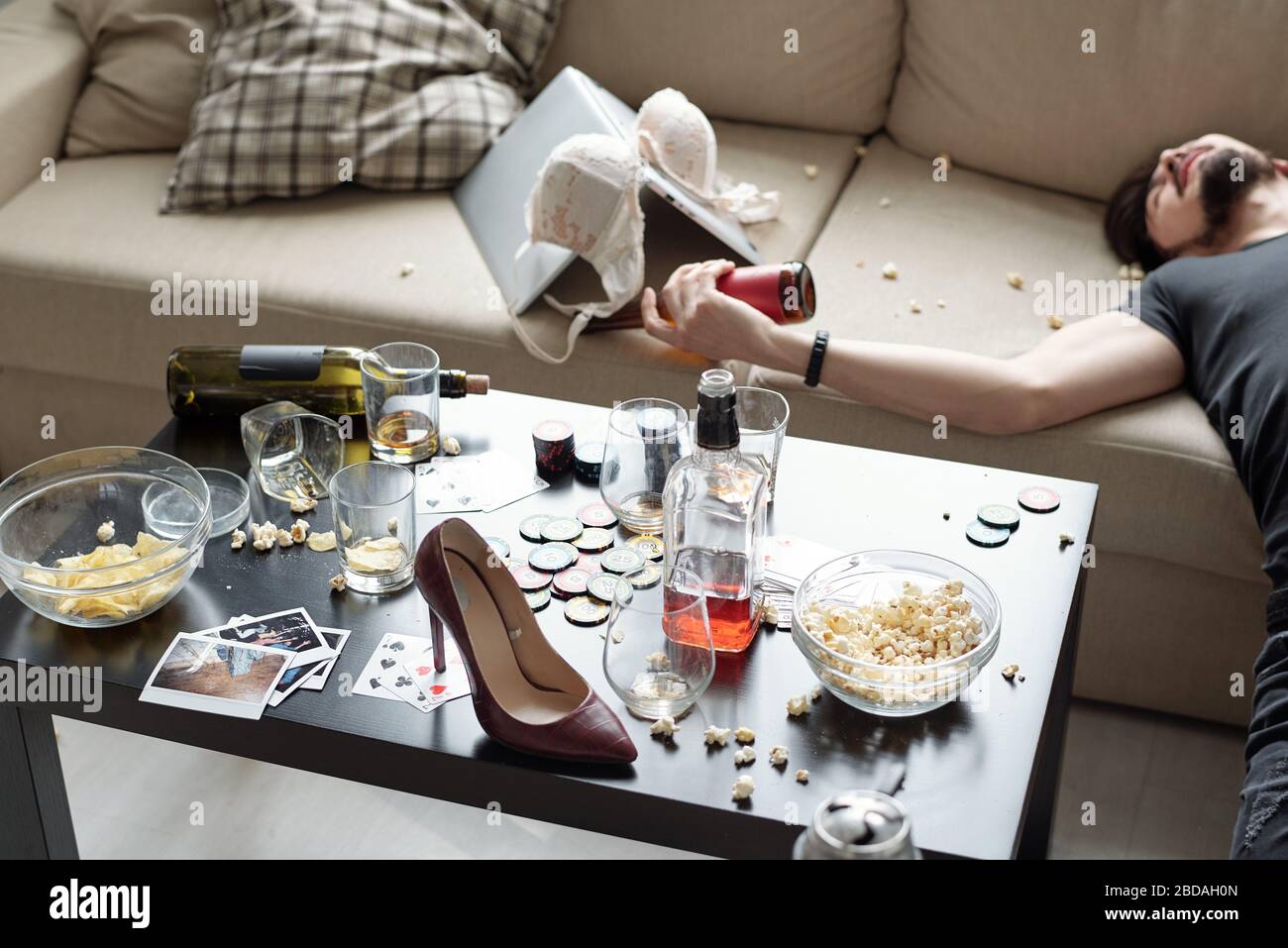 Drunken man sleeping with beer bottle with upper body on sofa in messy ...