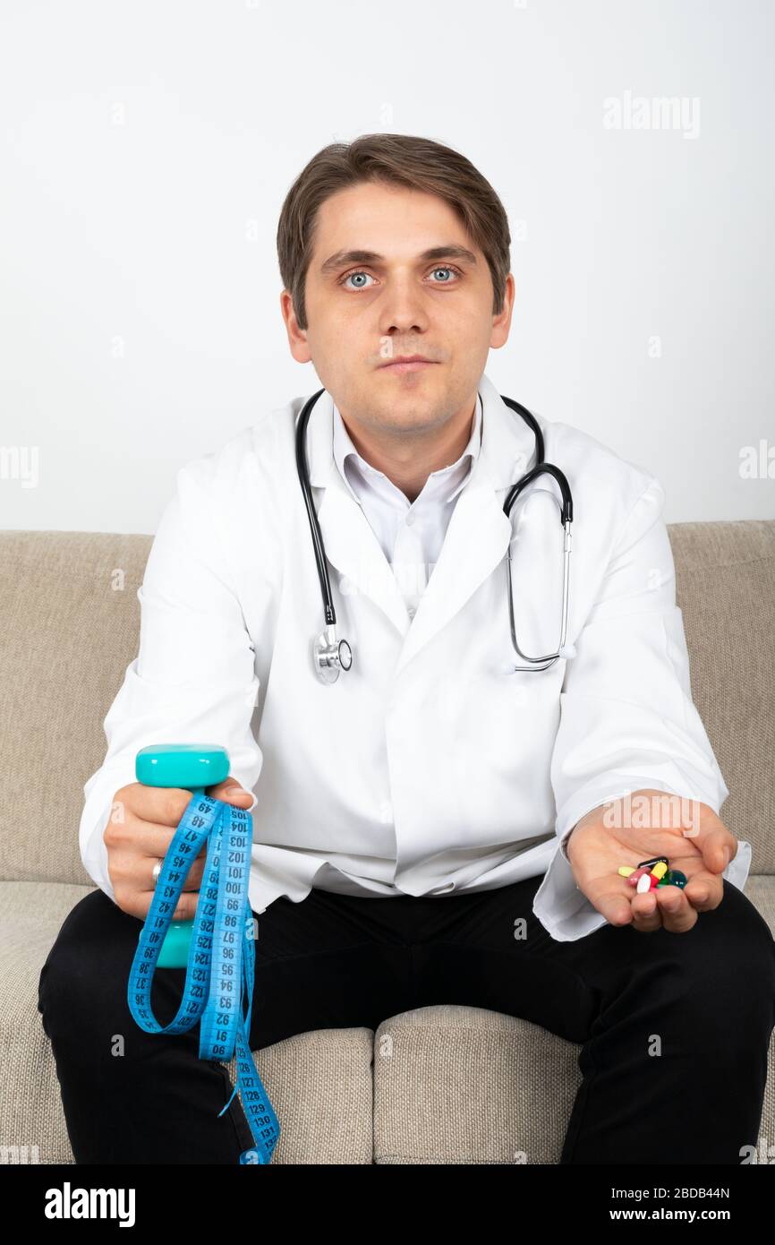 Young handsome doctor holding dietary supplements and fitness weight in ...