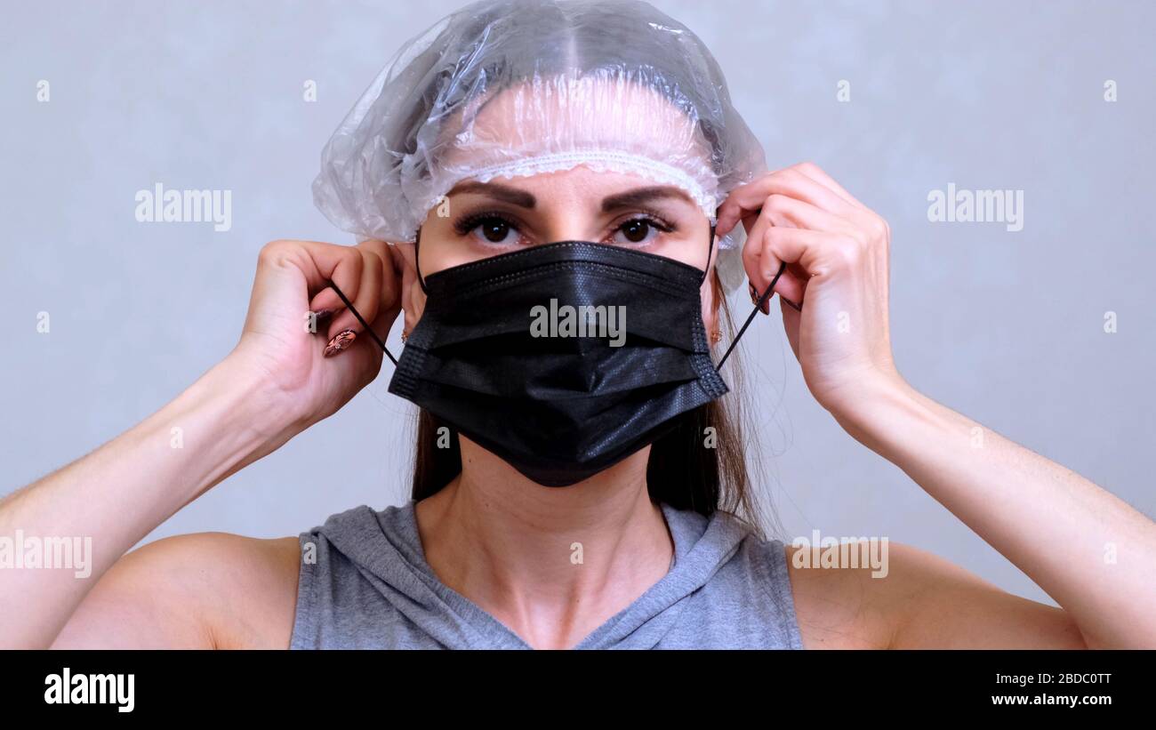 Female patient in a disposable cap puts on a black protective mask ...