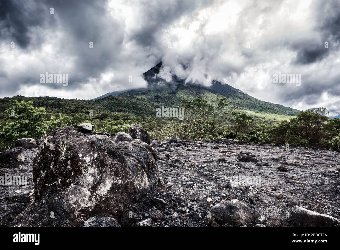 Volcanic stones with Arenal volcano nestled in the clouds in background ...