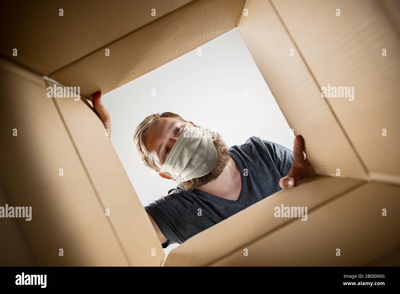 Young man opening the huge postal package wearing protective face mask ...