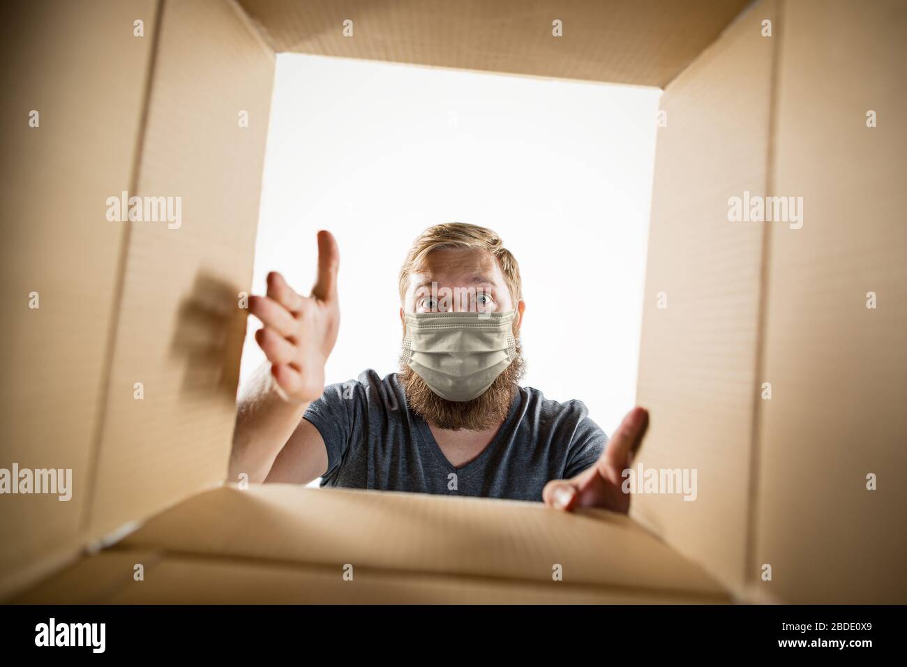 Young man opening the huge postal package wearing protective face mask ...