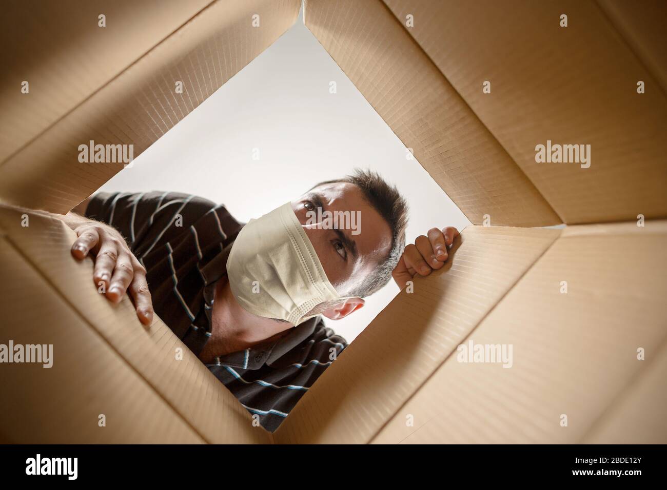 Young man opening the huge postal package wearing protective face mask ...