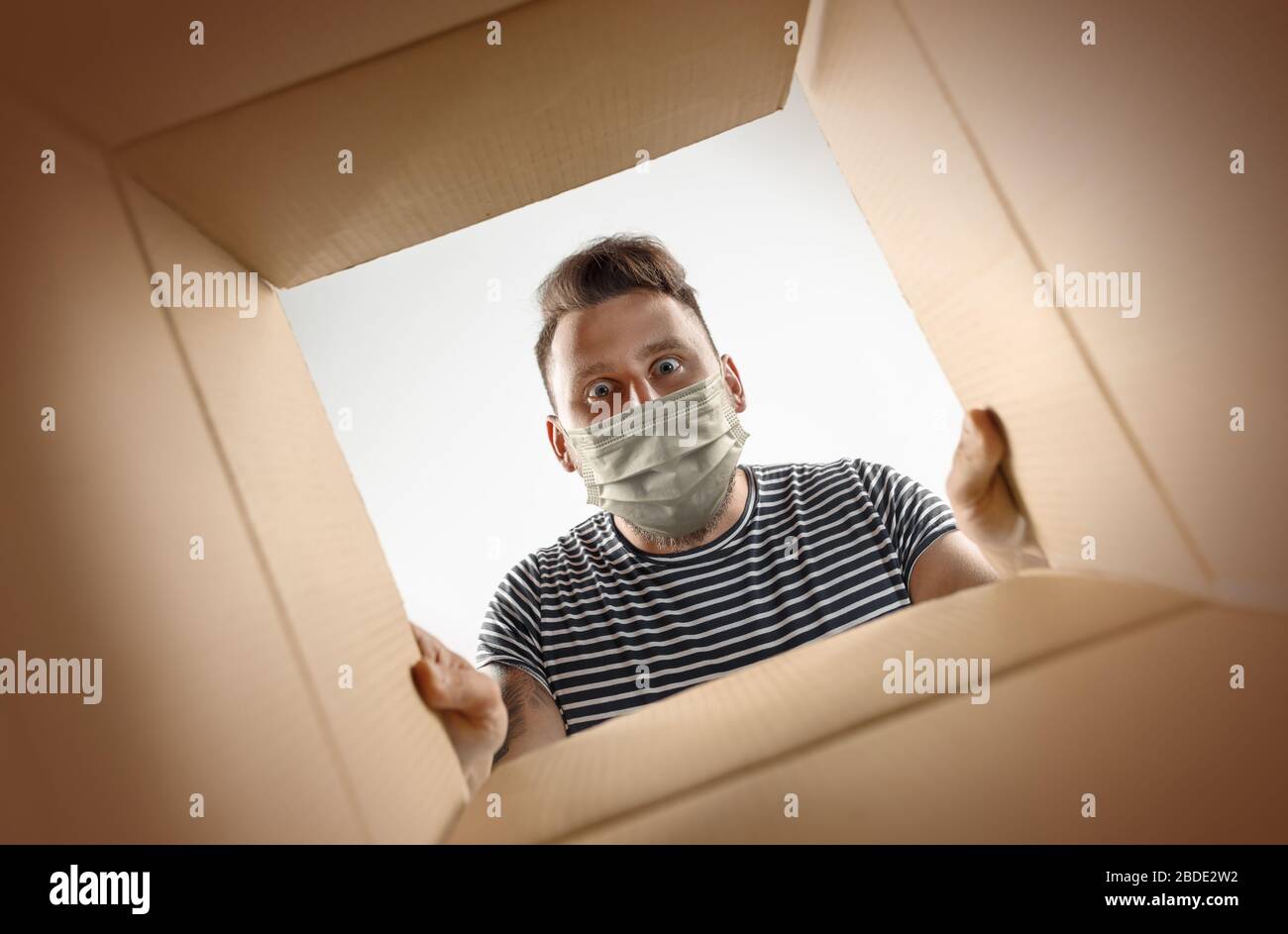 Young man opening the huge postal package wearing protective face mask ...