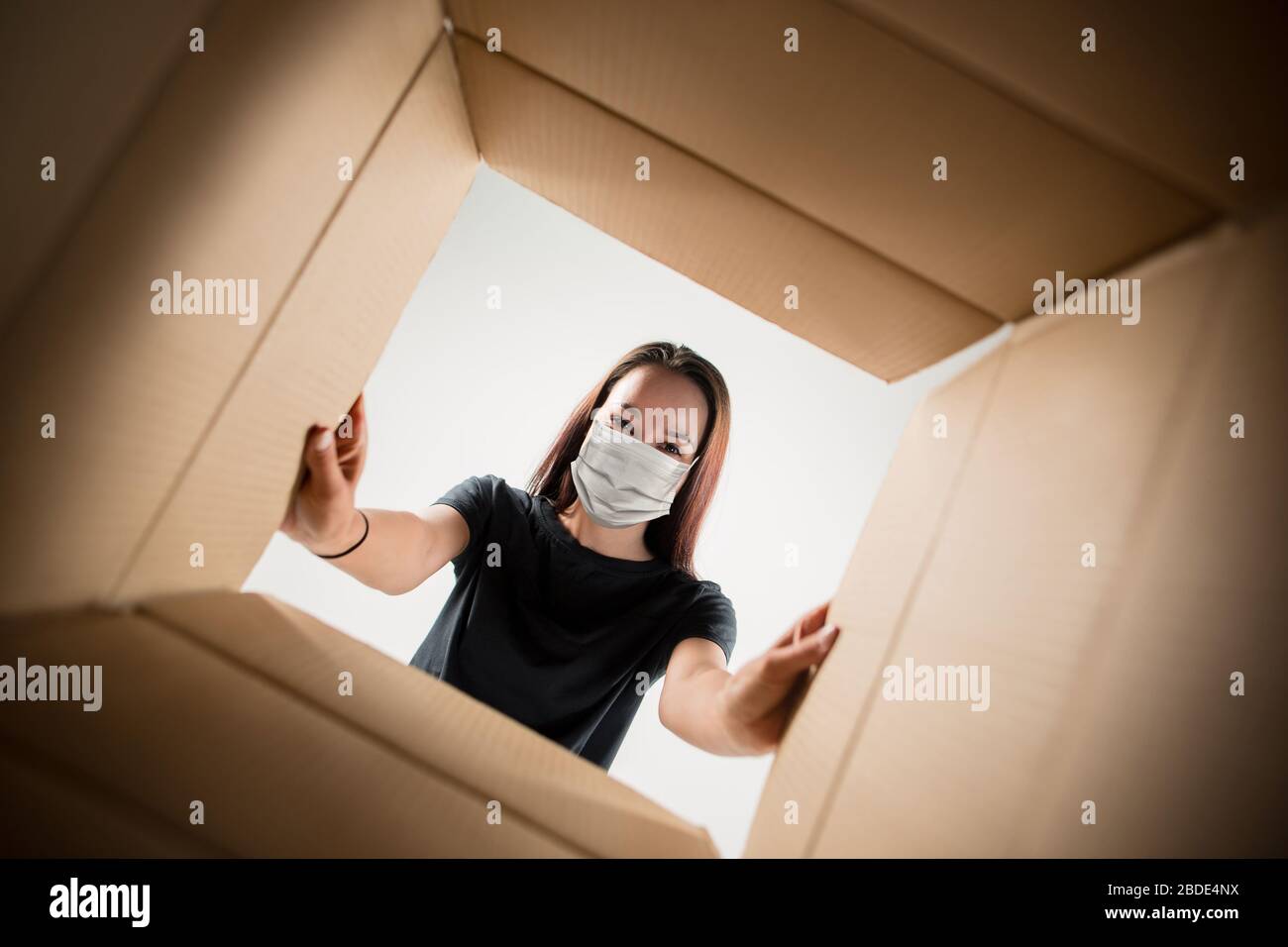 Young woman opening the huge postal package wearing protective face ...