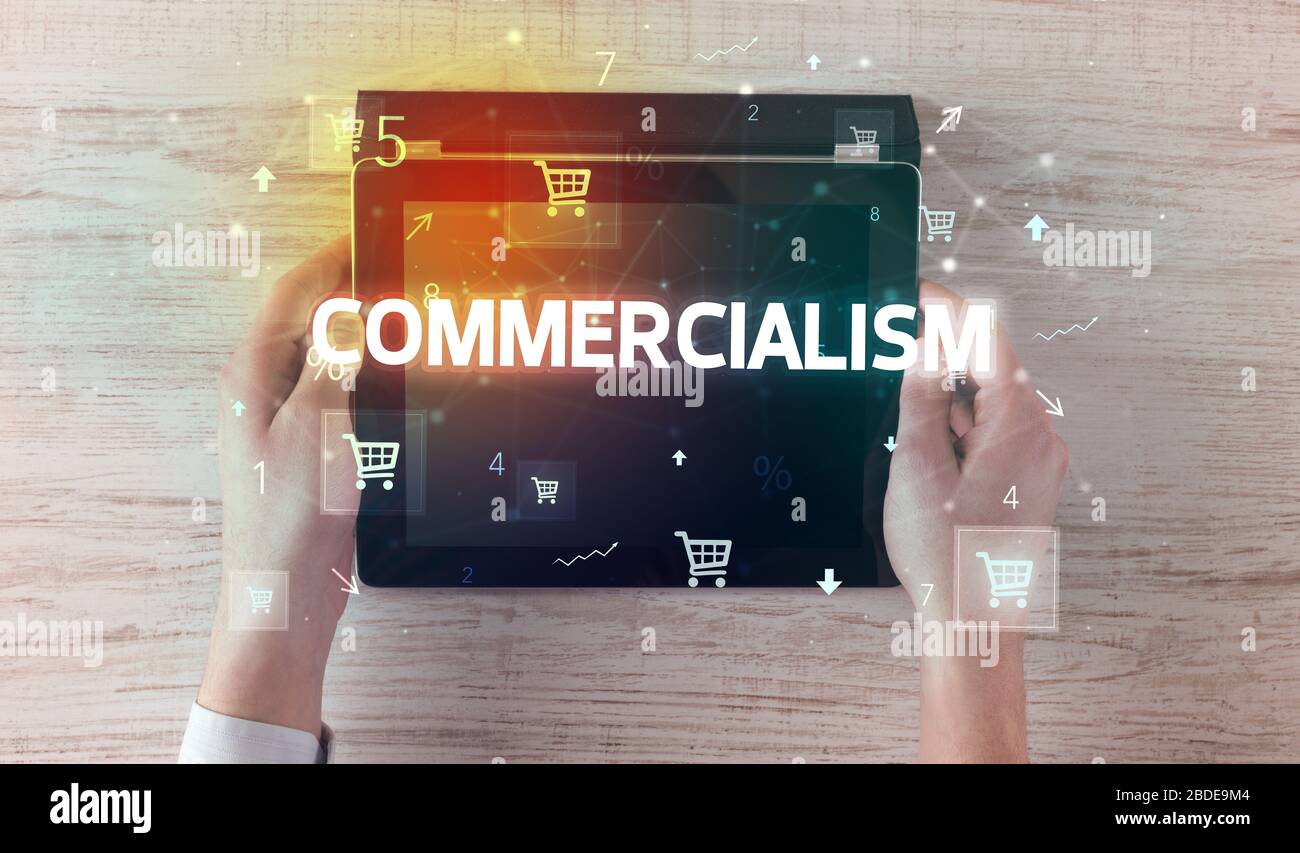 Close-up of a hand holding tablet with COMMERCIALISM inscription ...