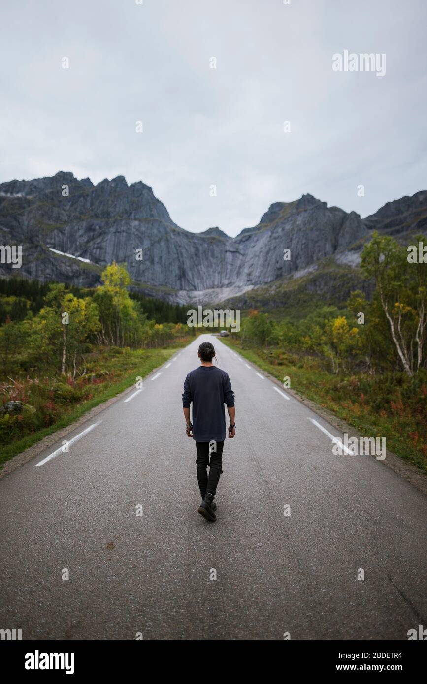 Norway, Lofoten Islands, Man walking down road in mountain landscape ...