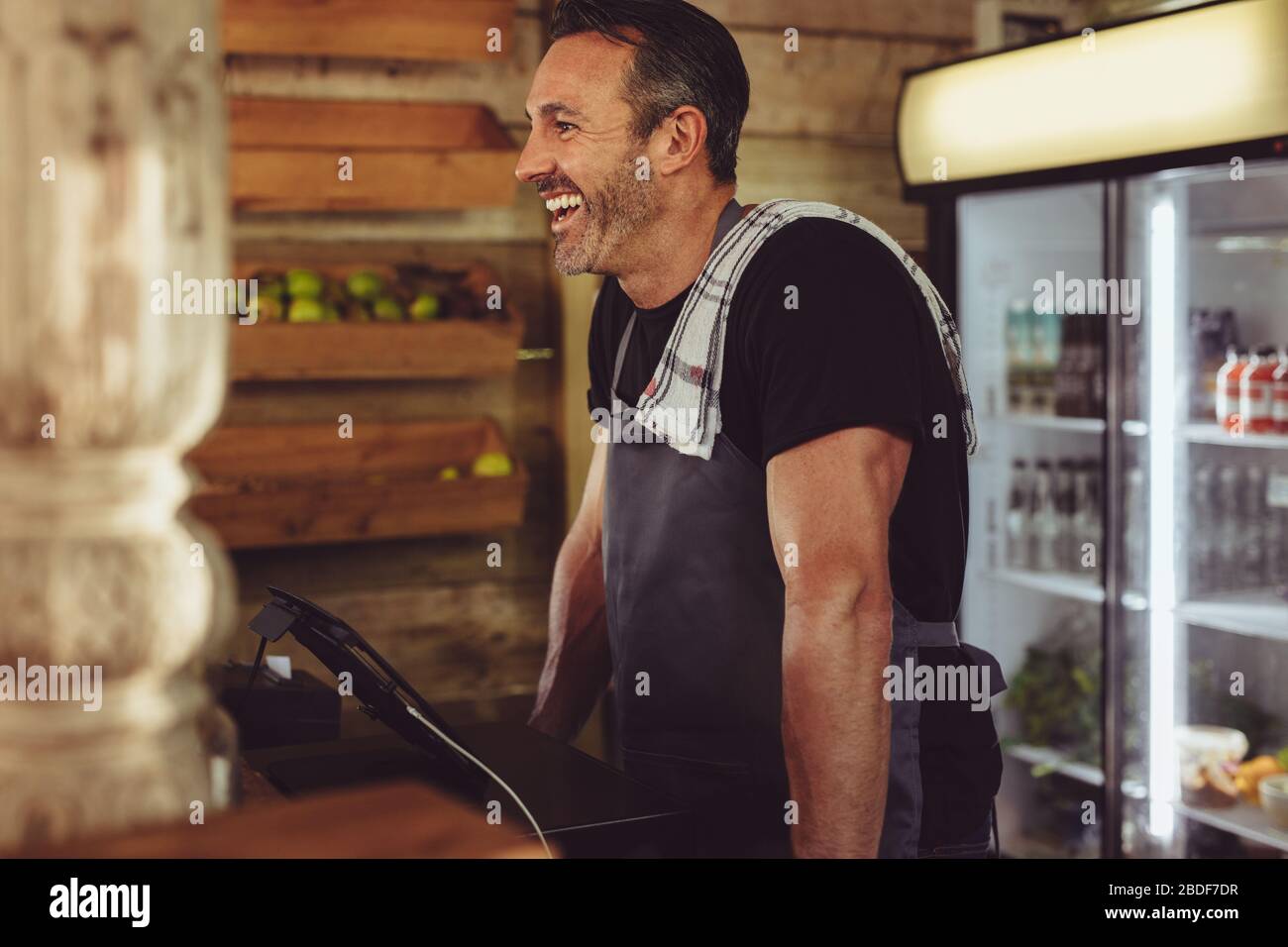 Cafe worker standing behind checkout counter and smiling. Barista with ...