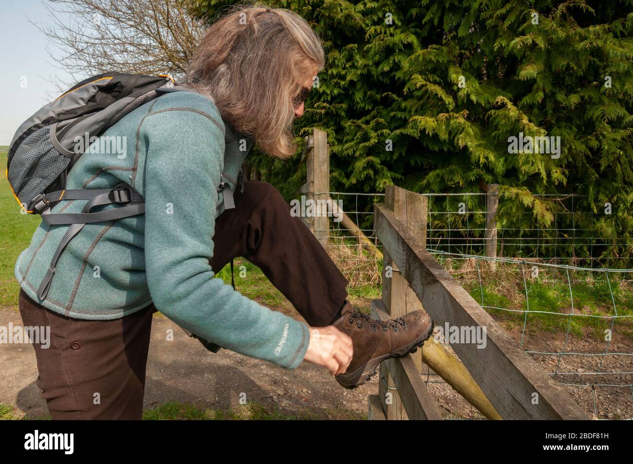 Woman walker tying up her laces while resting on a gate in the ...
