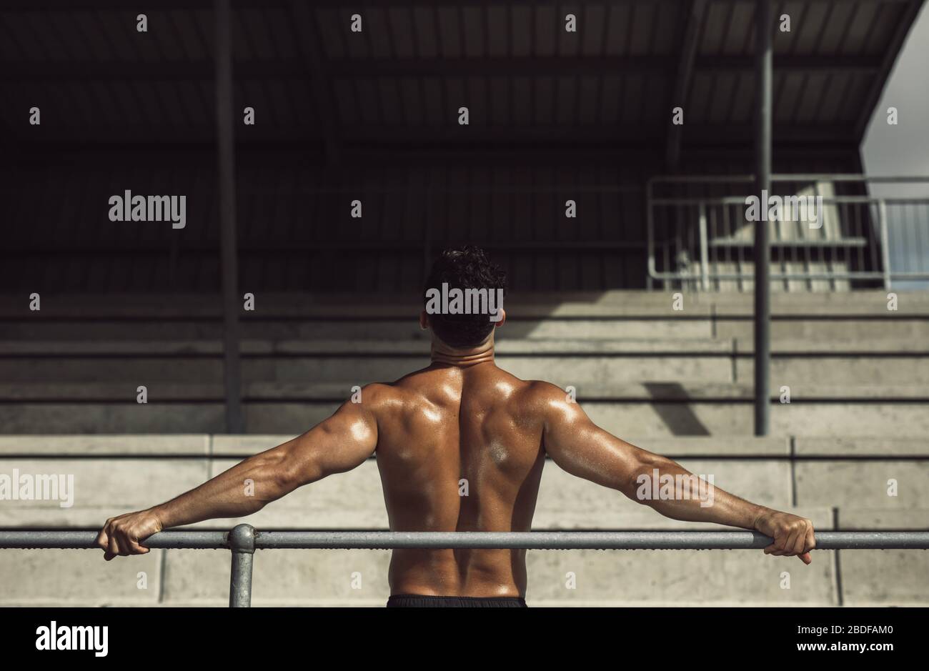 Rear view of muscular young man standing by a railing in stadium stands ...