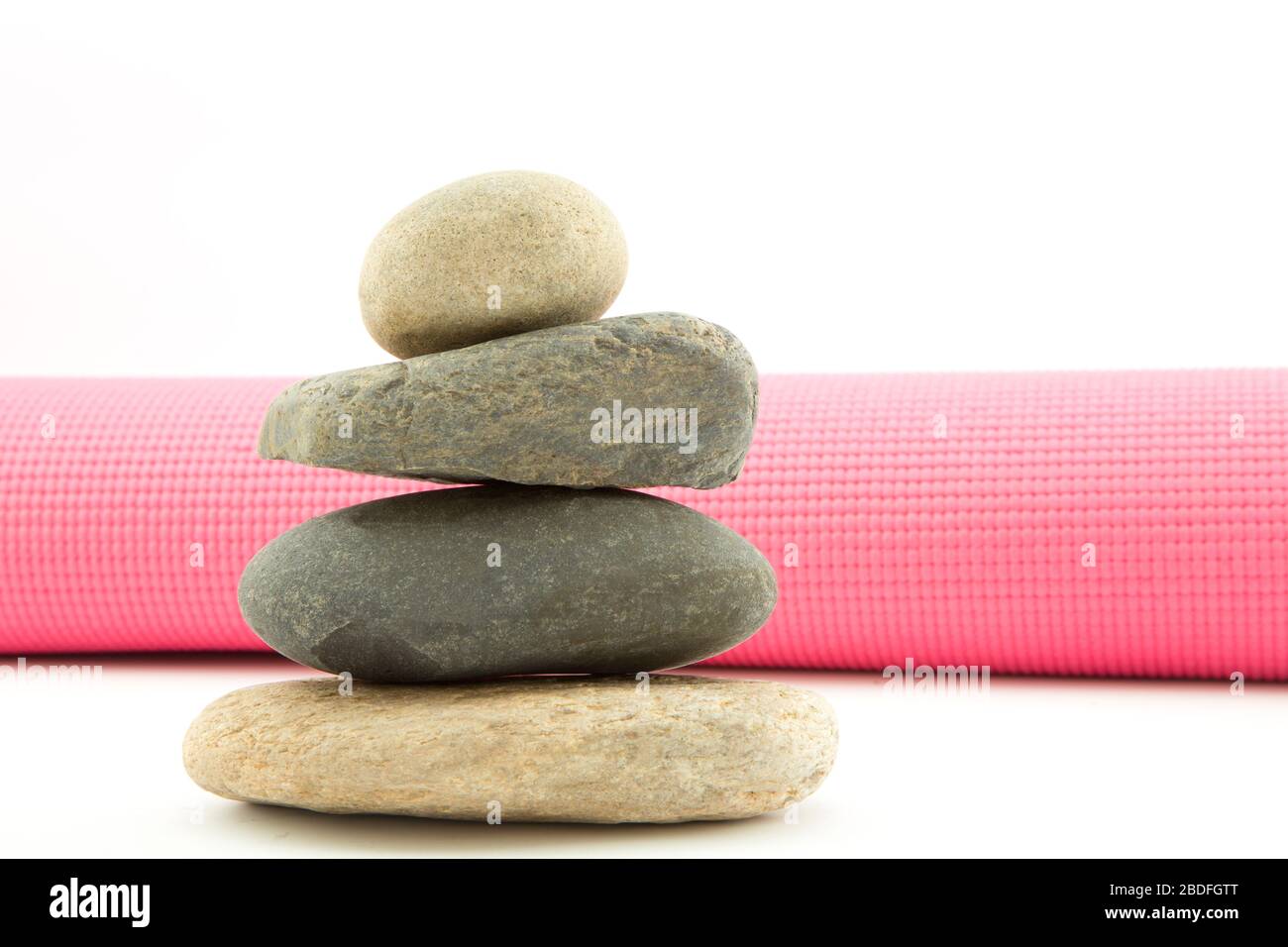 Four river rocks in Zen stack in front of pink yoga mat on white ...