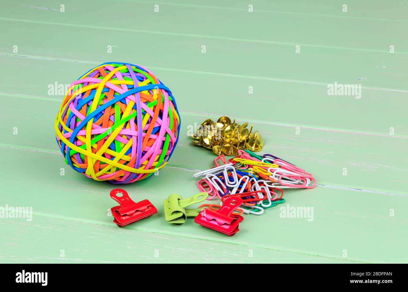 Coloured ball of rubber bands paper clips and drawing pins on a green ...