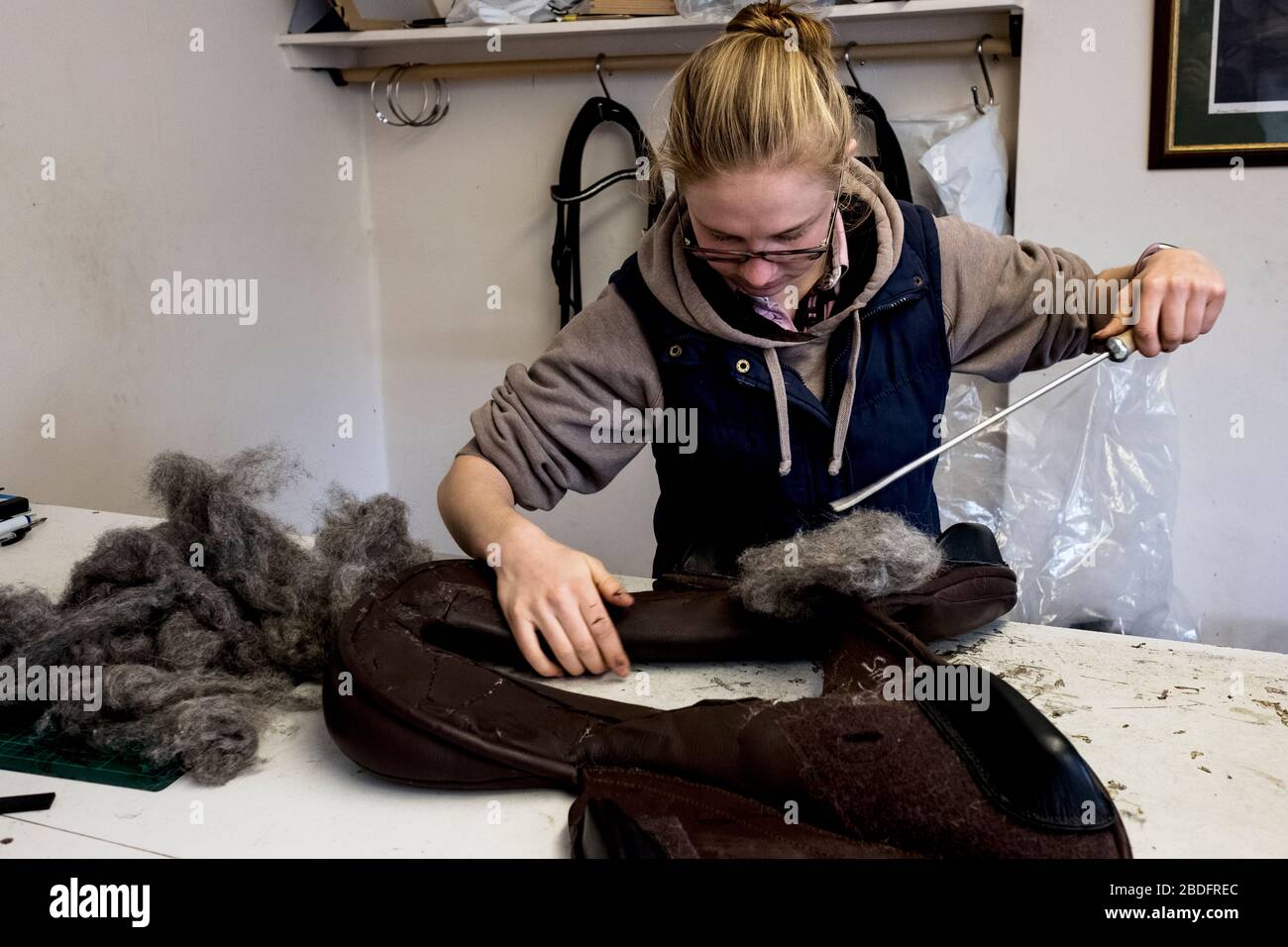 Female saddler standing in workshop, stuffing leather saddle with horse ...