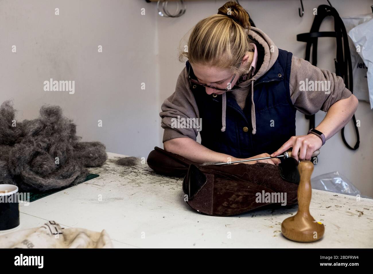 Female saddler standing in workshop, stuffing leather saddle with horse ...