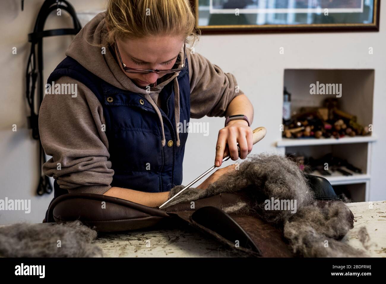 Female saddler standing in workshop, stuffing leather saddle with horse ...