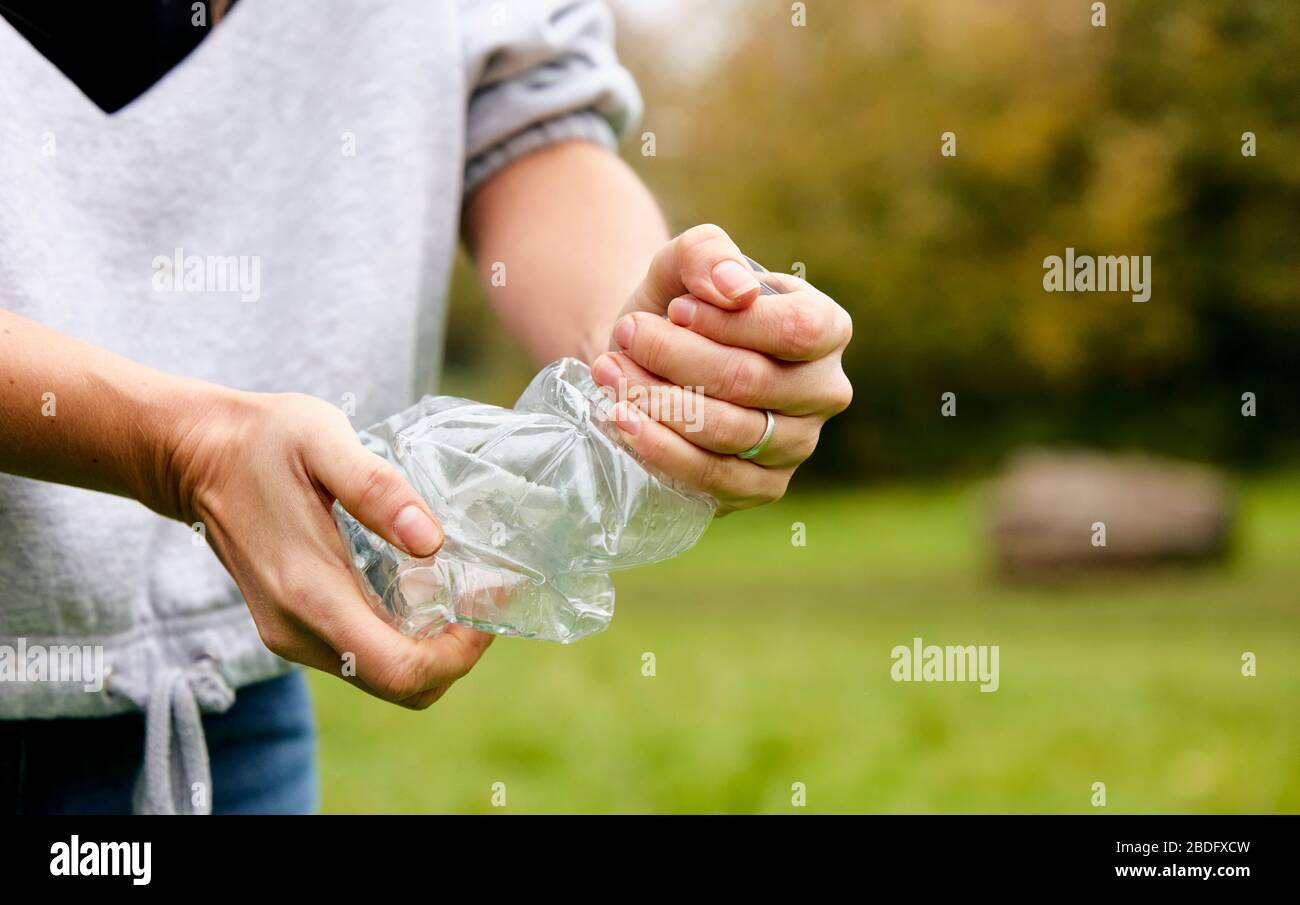 Woman stuffing soft waste plastics into large plastic bottle to make an ...