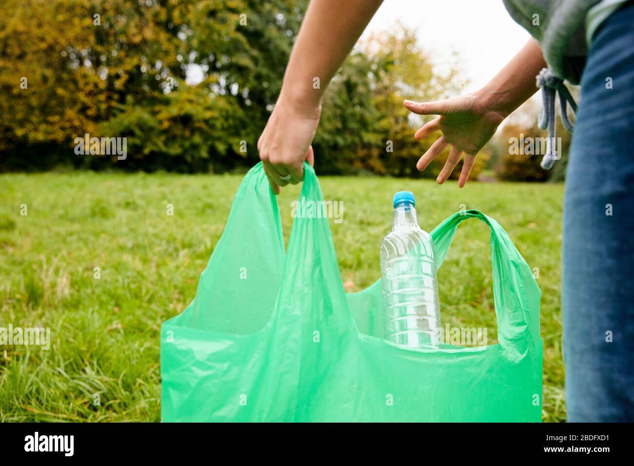 Woman stuffing soft waste plastics into large plastic bottle to make an ...