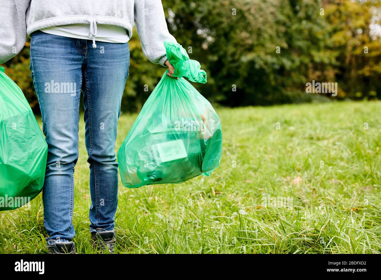 Woman stuffing soft waste plastics into large plastic bottle to make an ...