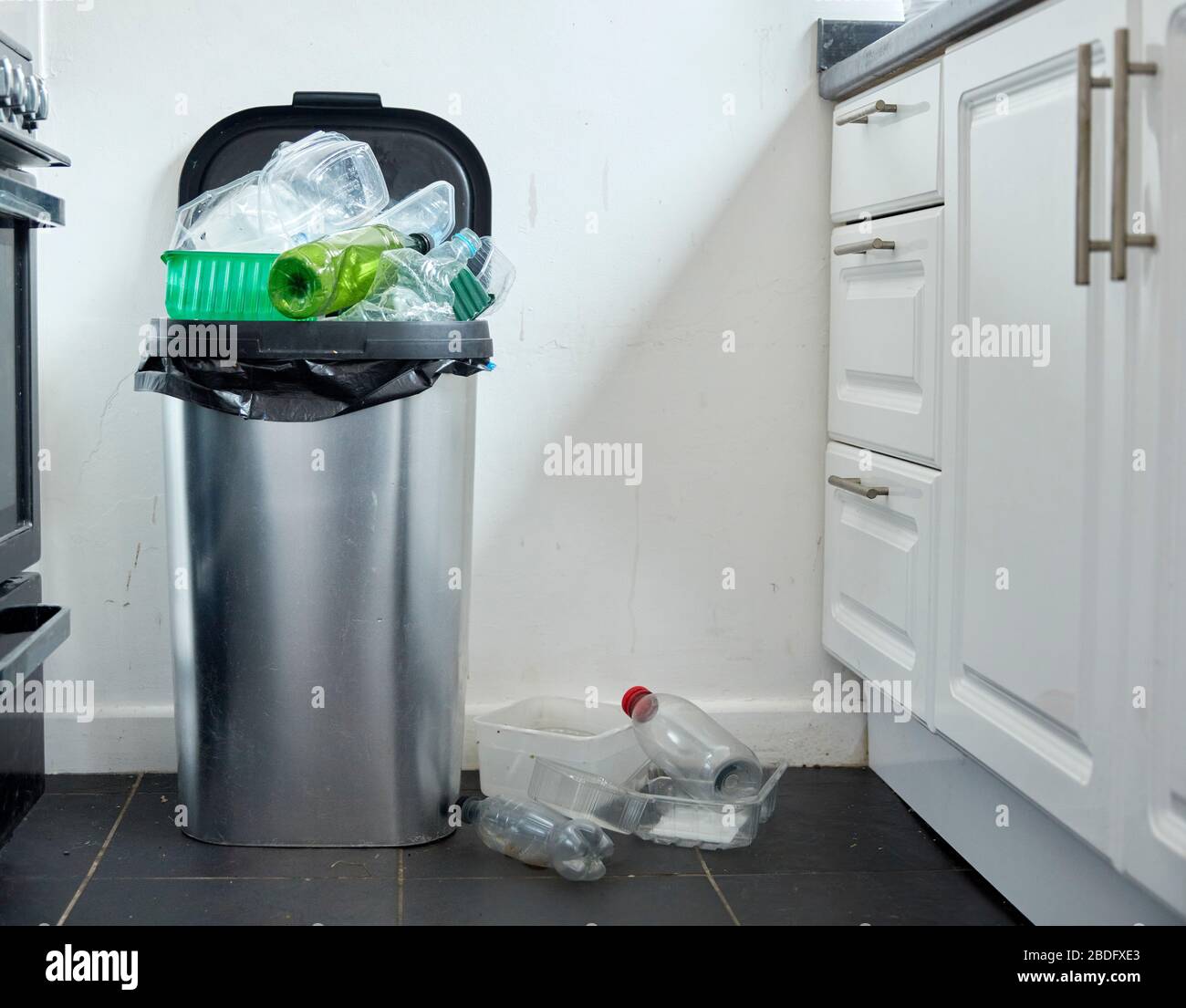 Various used plastic containers overflowing from dustin in kitchen ...