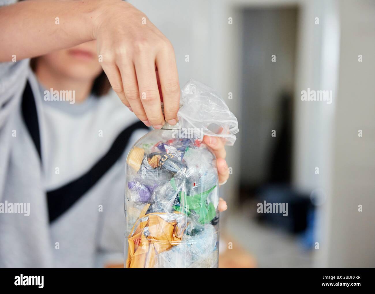 Woman stuffing soft waste plastics into large plastic bottle to make an ...