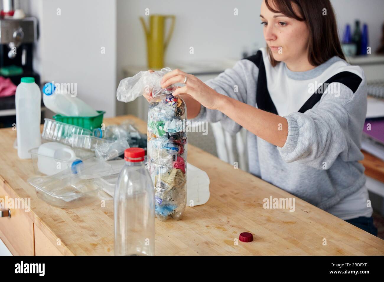 Woman stuffing soft waste plastics into large plastic bottle to make an ...