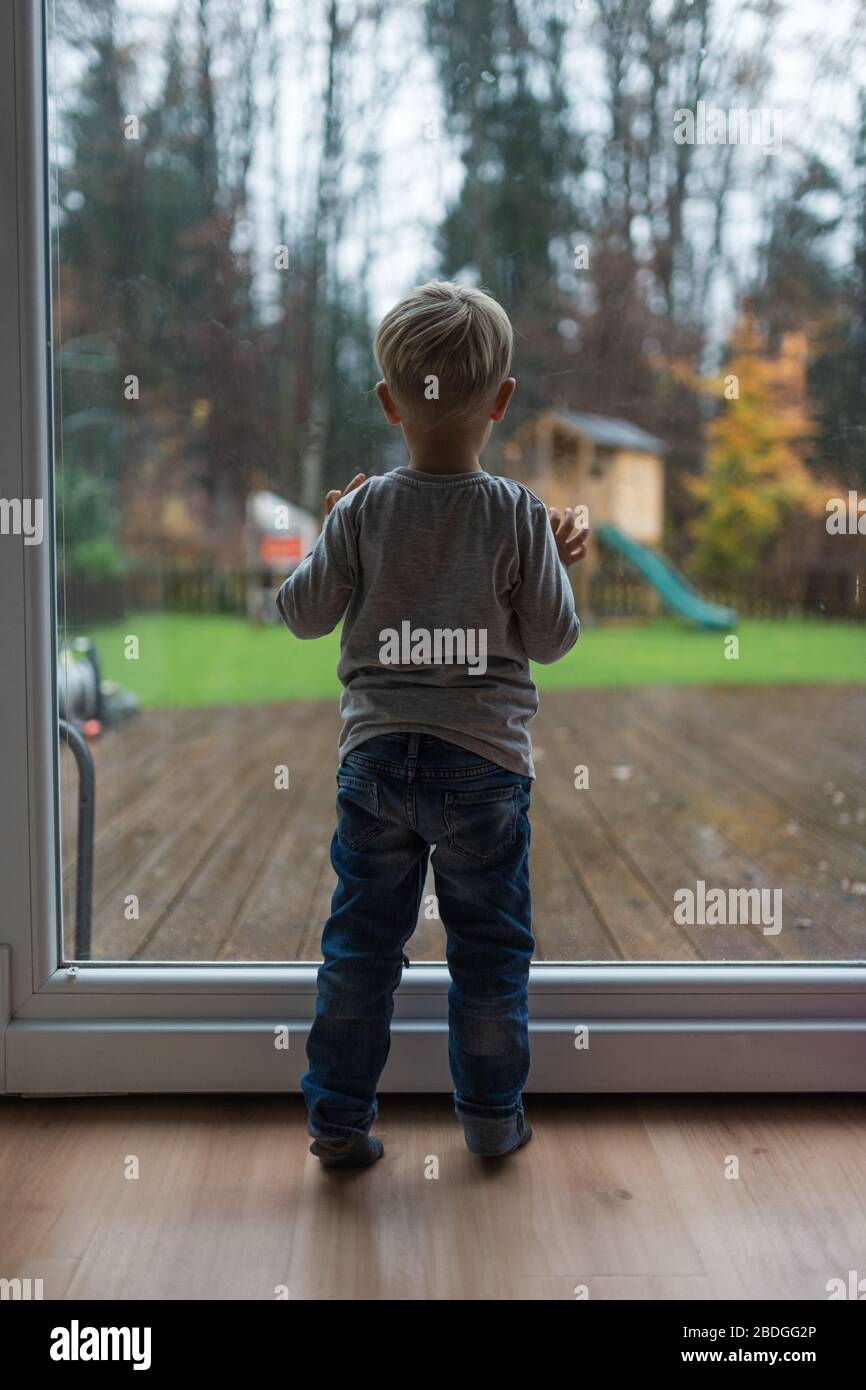 View from behind of a little toddler boy standing by a glass door ...