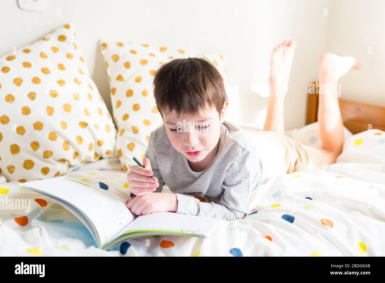 School Boy on bed and doing school homework at home, writing in ...