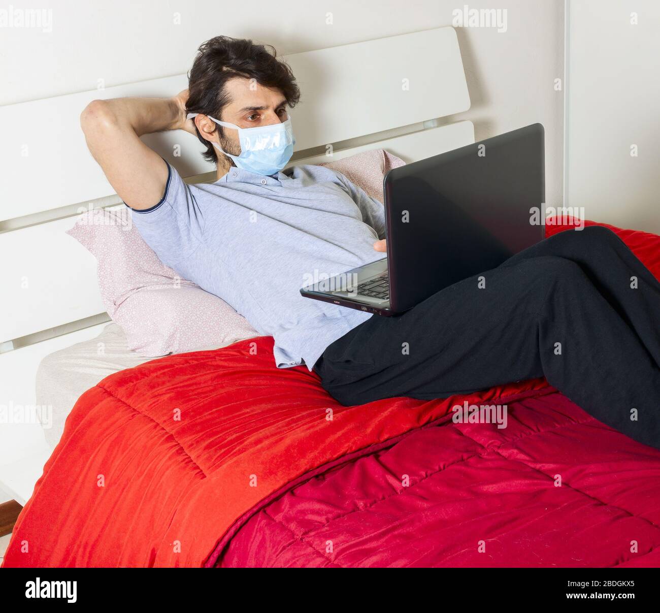 Sick man with medical mask using tablet pc in bed. Home quarantine ...
