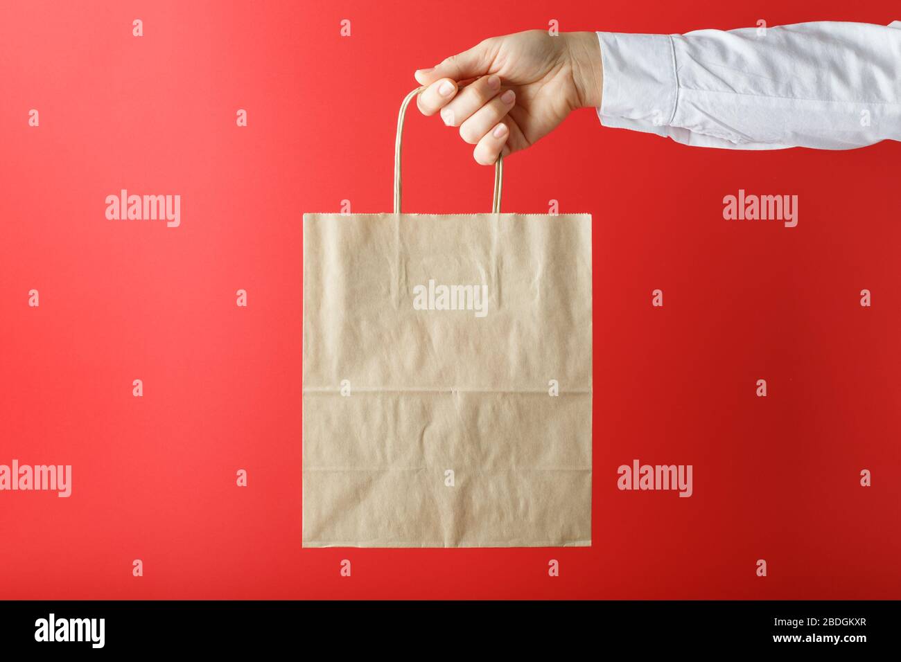 Brown paper bag at arm's length, on a red background Stock Photo - Alamy