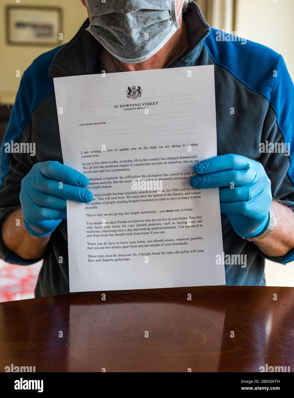 Man wearing surgical gloves and face mask holding HM Government letter ...