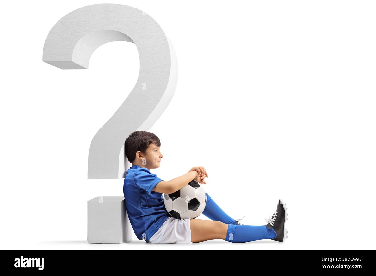 Young boy sitting on the floor holding a football and leaning on a ...