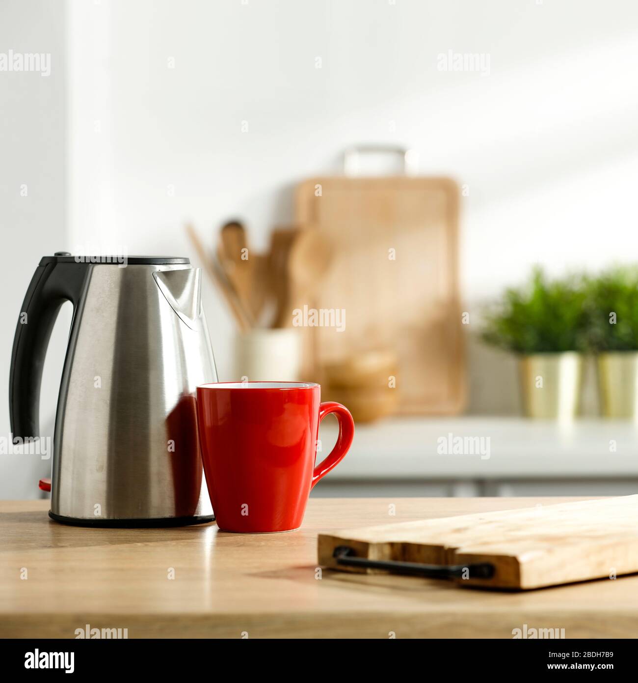 Electric kettle and red mug on wooden table in nice cozy kitchen ...