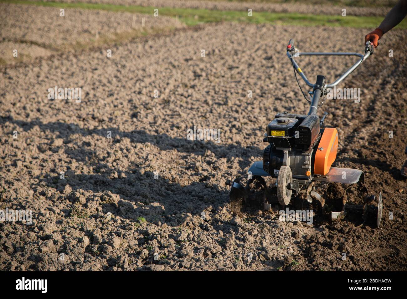 small orange plowing machine in hands of a farmer making arable in ...