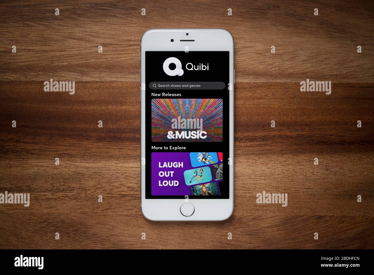An iPhone showing the Quibi app rests on a plain wooden table ...