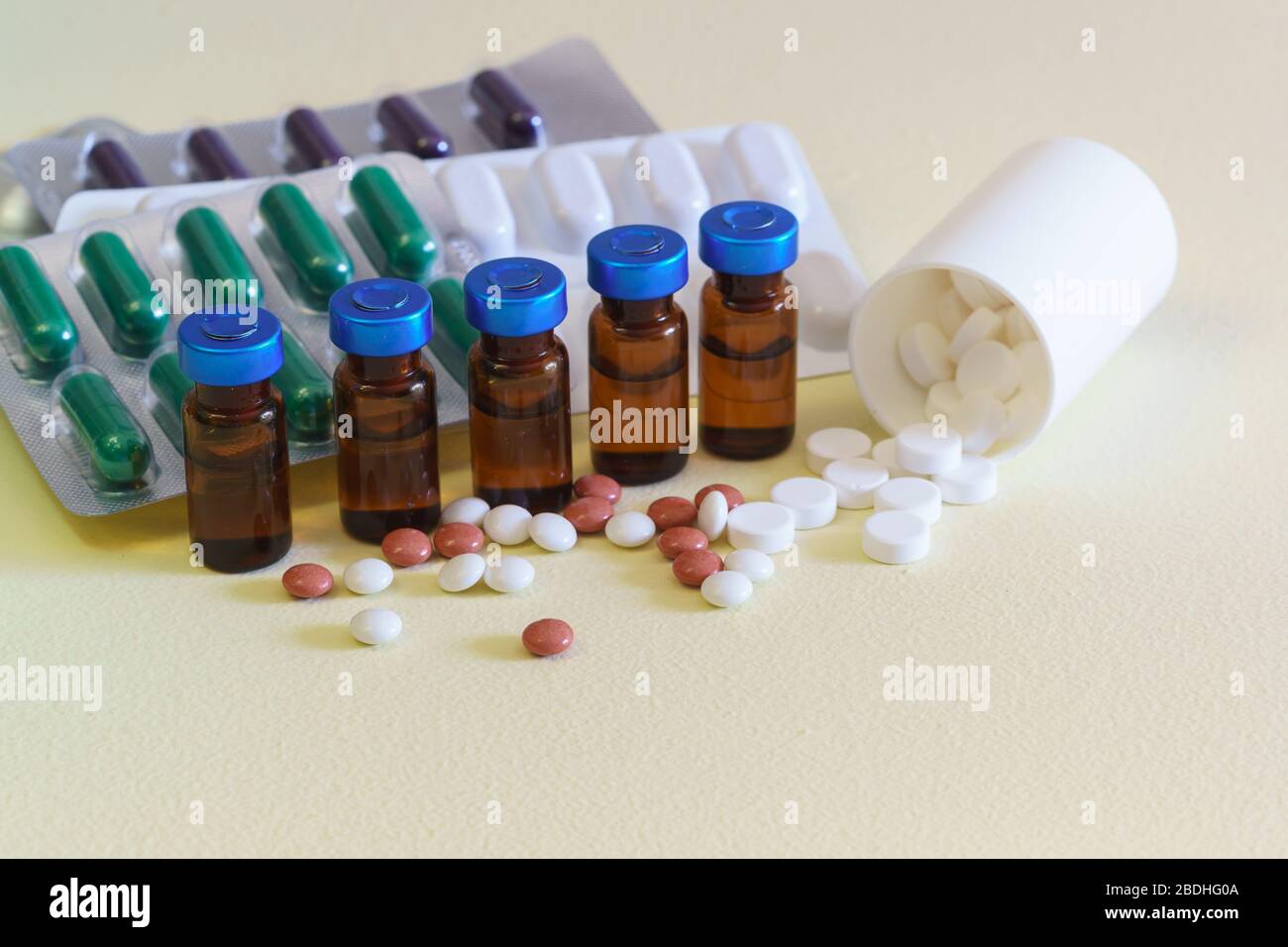 Vials of injectable drugs and scattered pills on a yellow table. Modern ...