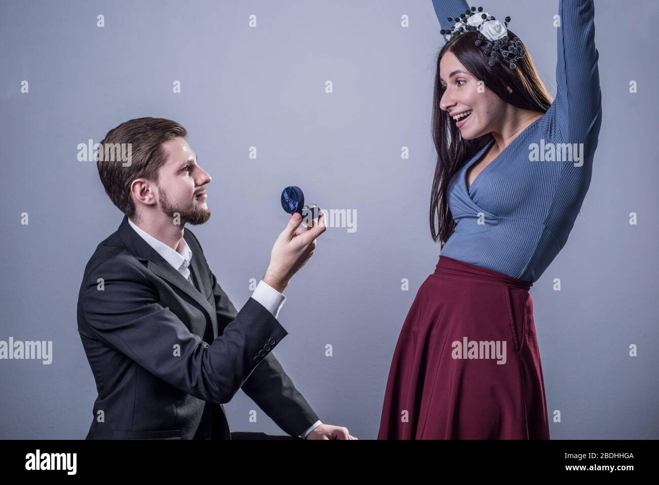 Studio portrait of a guy kneeling, makes a proposal with a ring to a ...