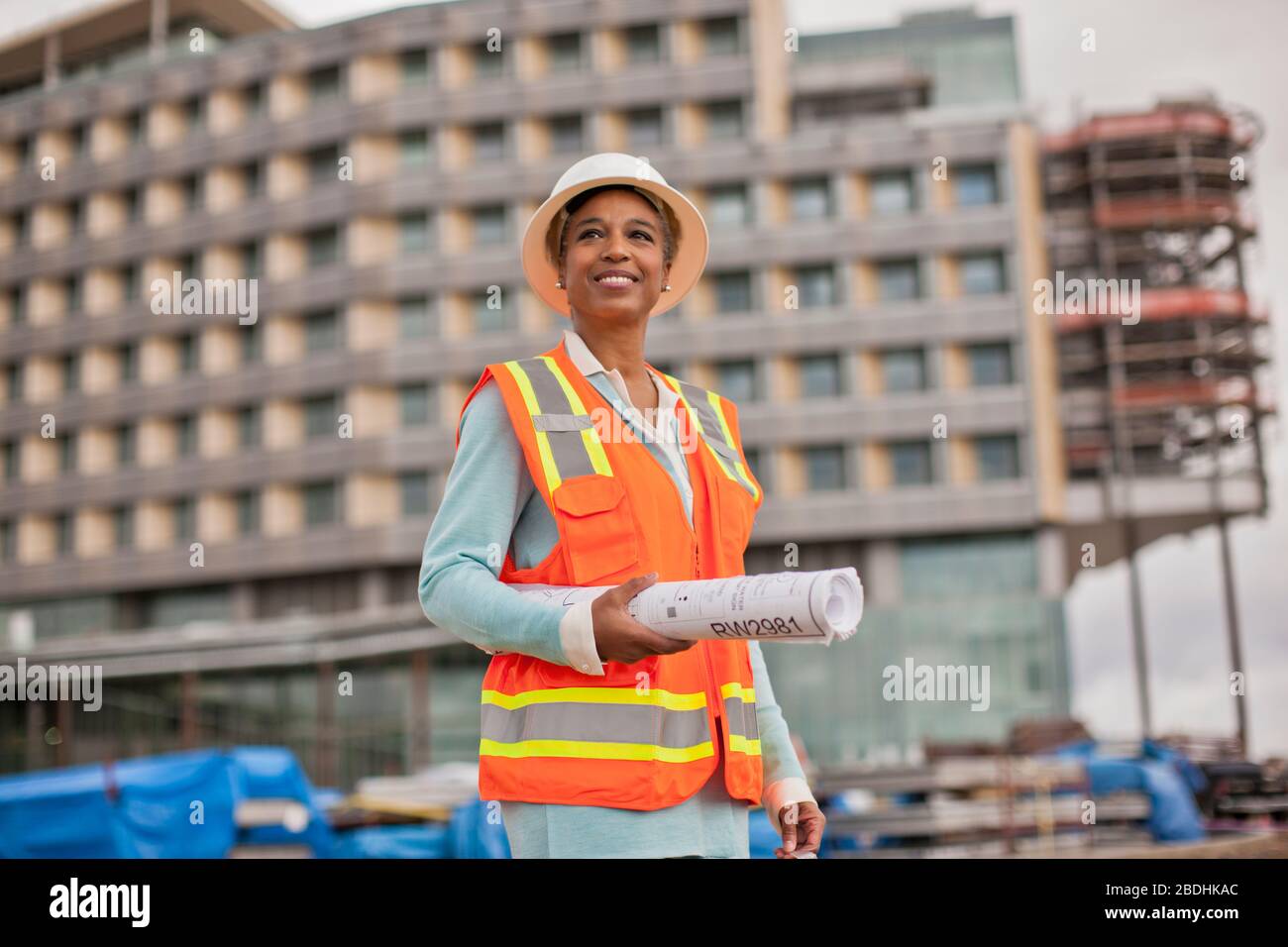 Proud young female engineer holding a roll of building plans on a ...