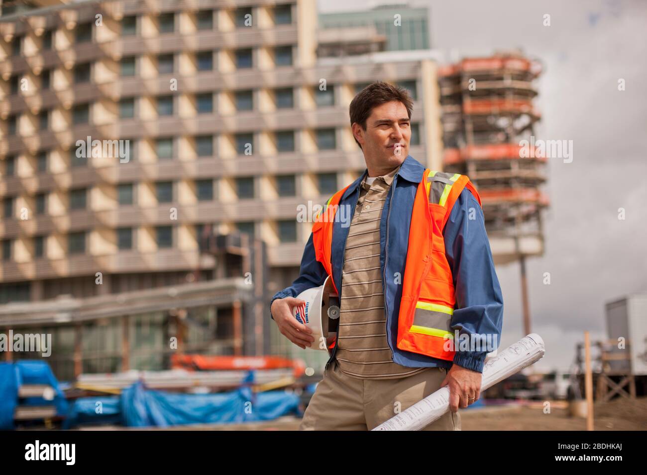 Handsome young architect in a high visibility vest holds his hardhat ...