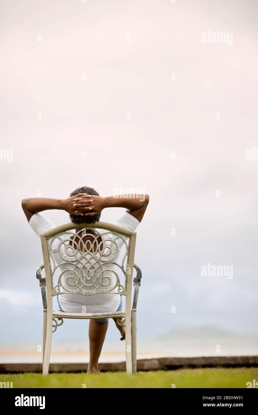 Mid-adult woman sitting in an outdoor chair with her hands behind her ...