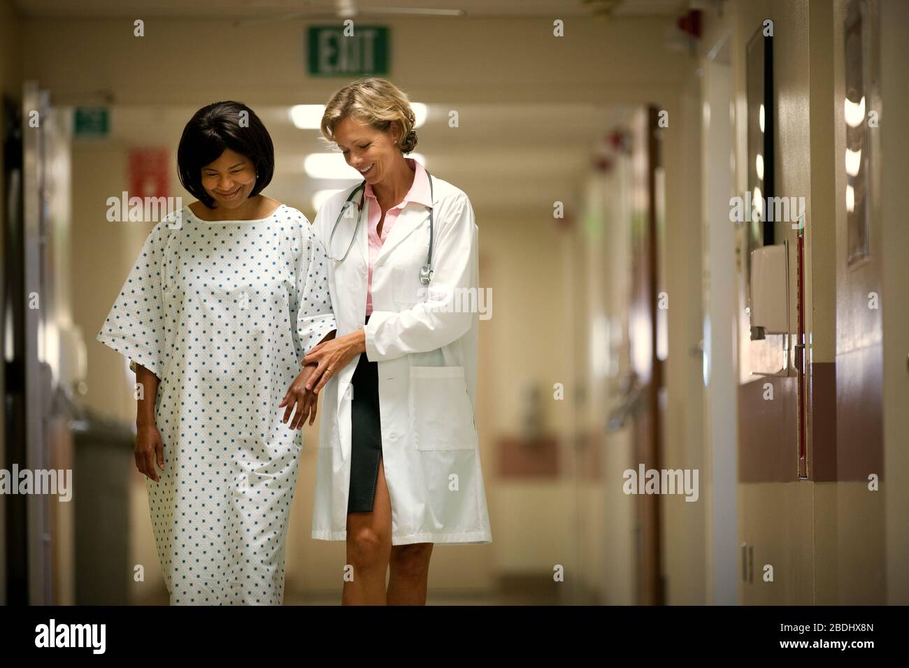 Doctor helping her patient to walk down the corridor for the first time ...