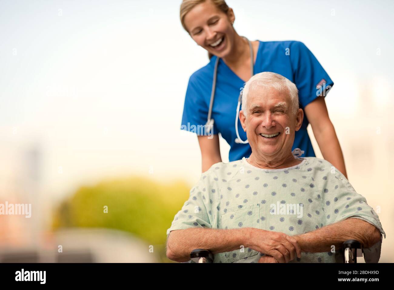 Young doctor and her elderly patient laughing together as she pushes ...